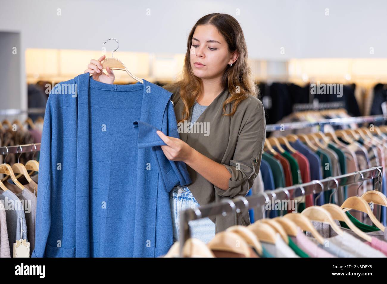 Focused young woman is thinking about buying a blue cardigan while ...