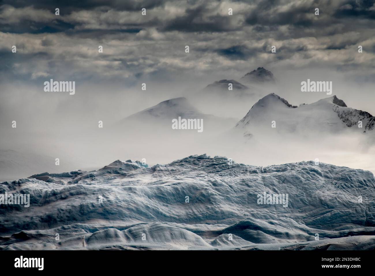 Iceberg in the foreground acts like a stage for wind-whipped snow ...