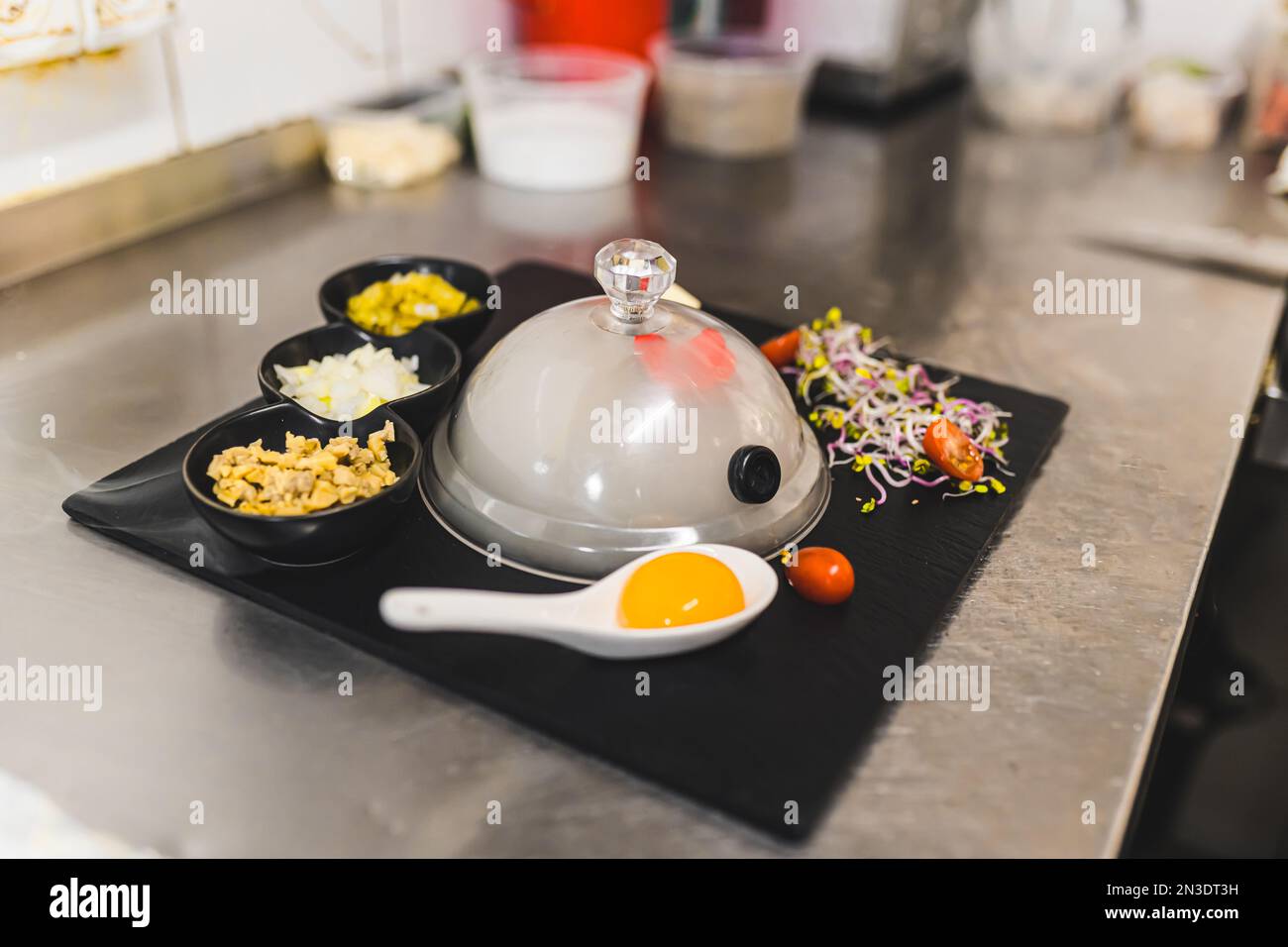 Plating smoked beef tartare under glass lid on black wooden board with ...