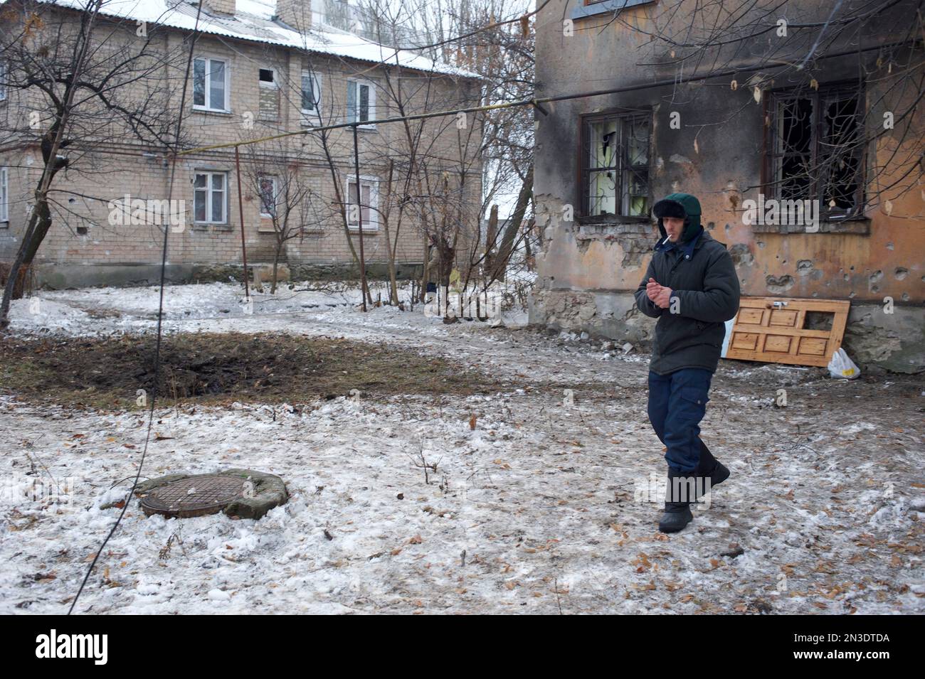 A man walks past a mortar impact site outside a damaged building in ...