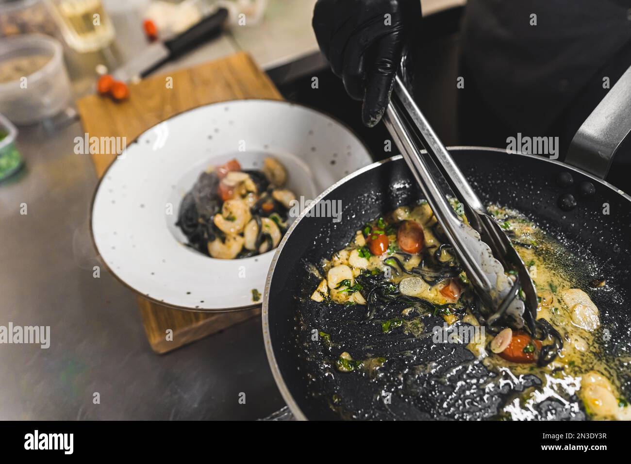 Unrecognisable person transferring black tagliolini pasta in shrimp ...