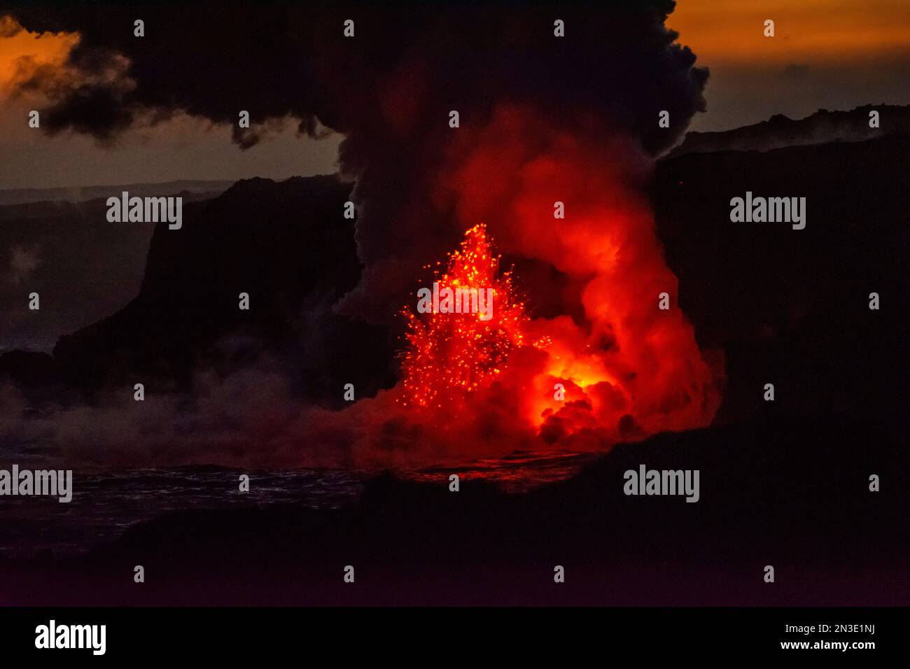 Red, hot lava spews on the ocean shoreline illuminating a huge column ...