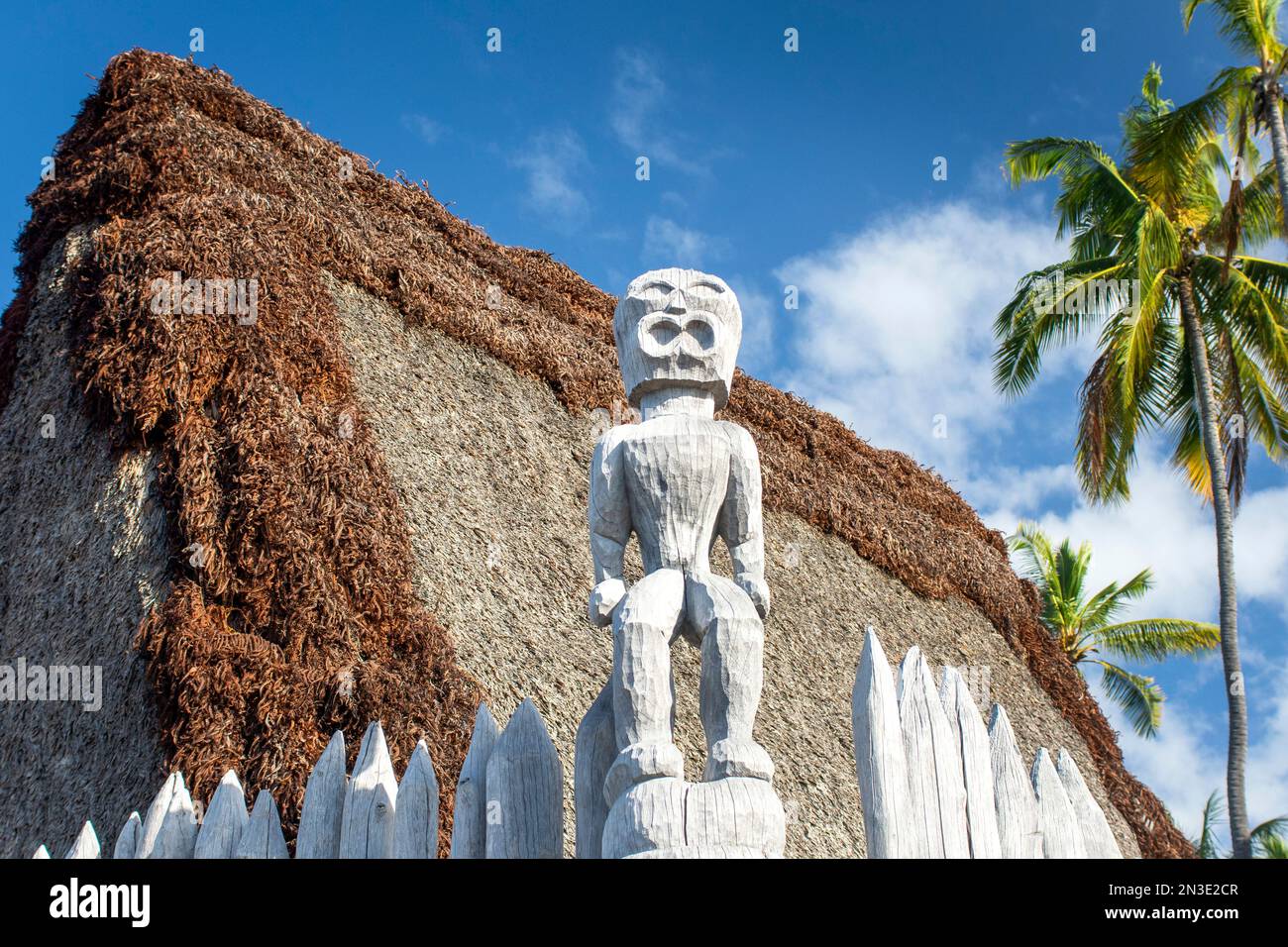 Wooden statue (Ki'i) of a Hawaiian deity in front of a thatched roof ...