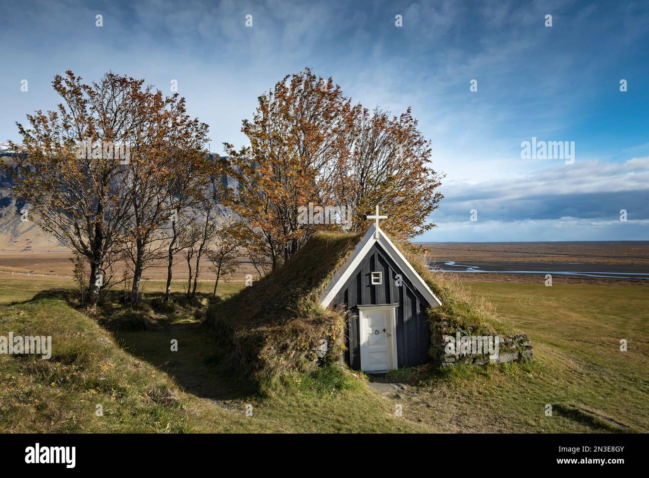 Small church painted black with a grass roof by some trees in autumn ...