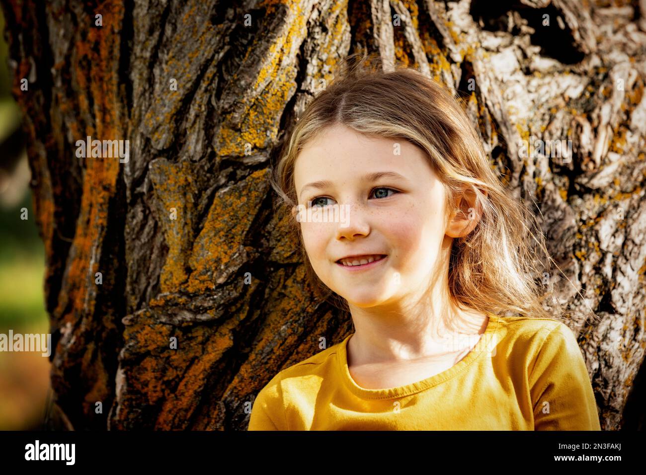 Young girl playing near a tree and pausing for a moment in a city park ...