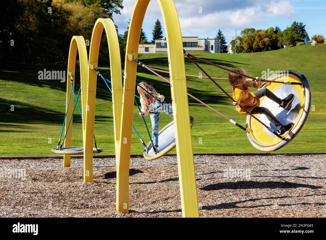 Young girls swinging on saucer swings in a playground on a warm fall ...