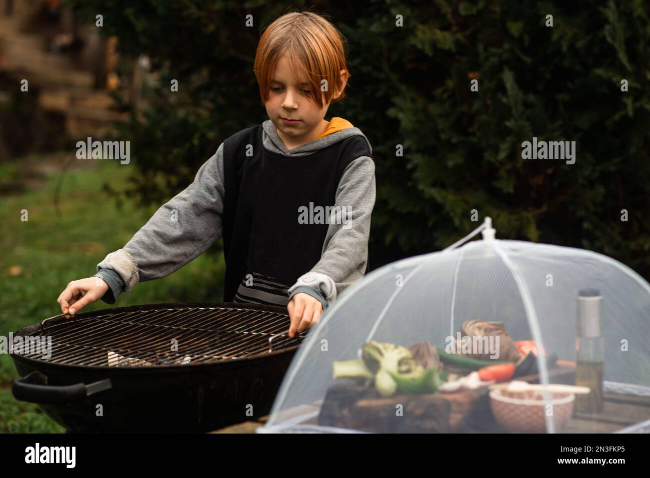 The boy prepares a round grill for grilling Stock Photo - Alamy