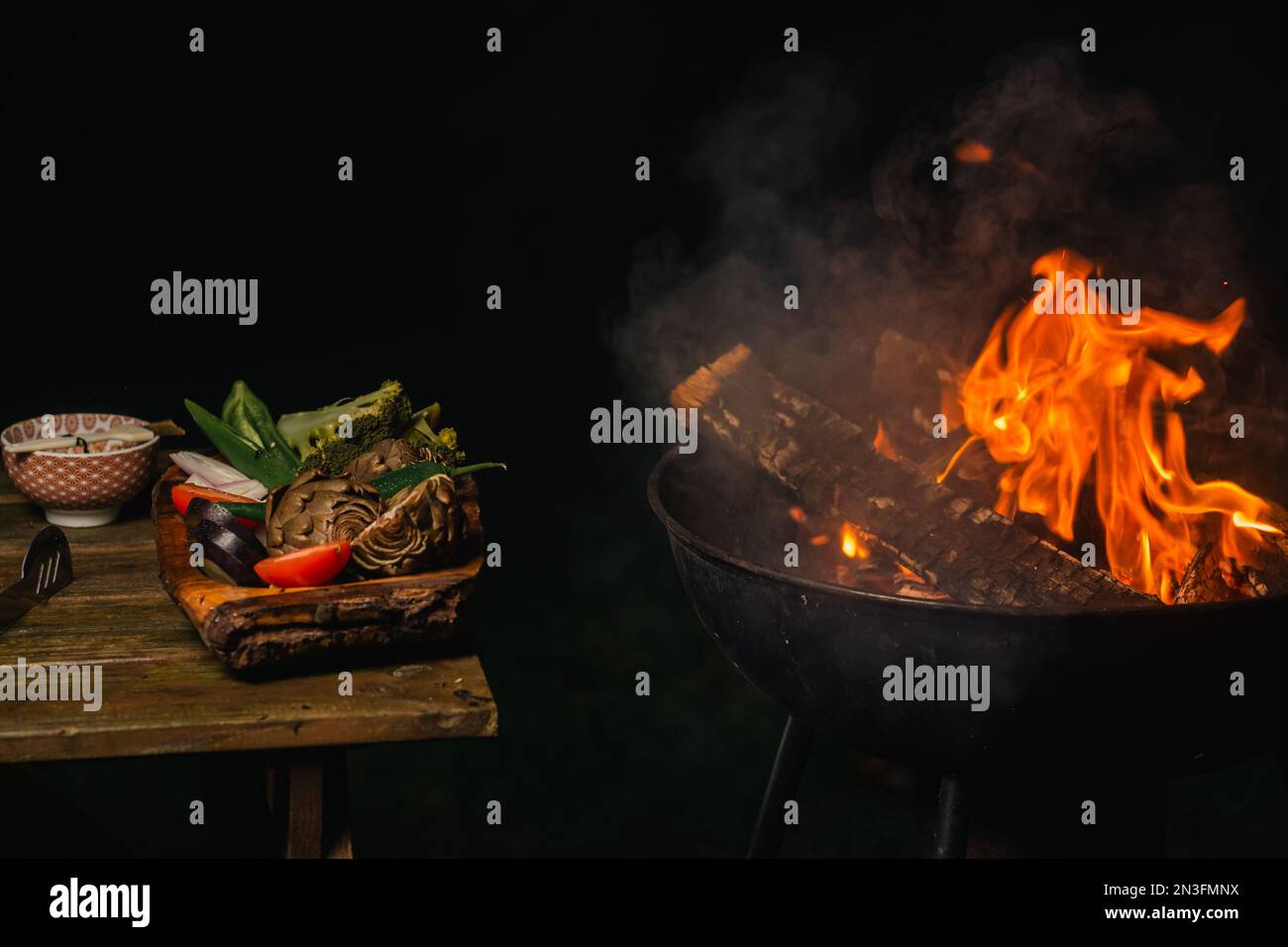 Burning round brazier and grilled vegetables. Evening time. Dark ...