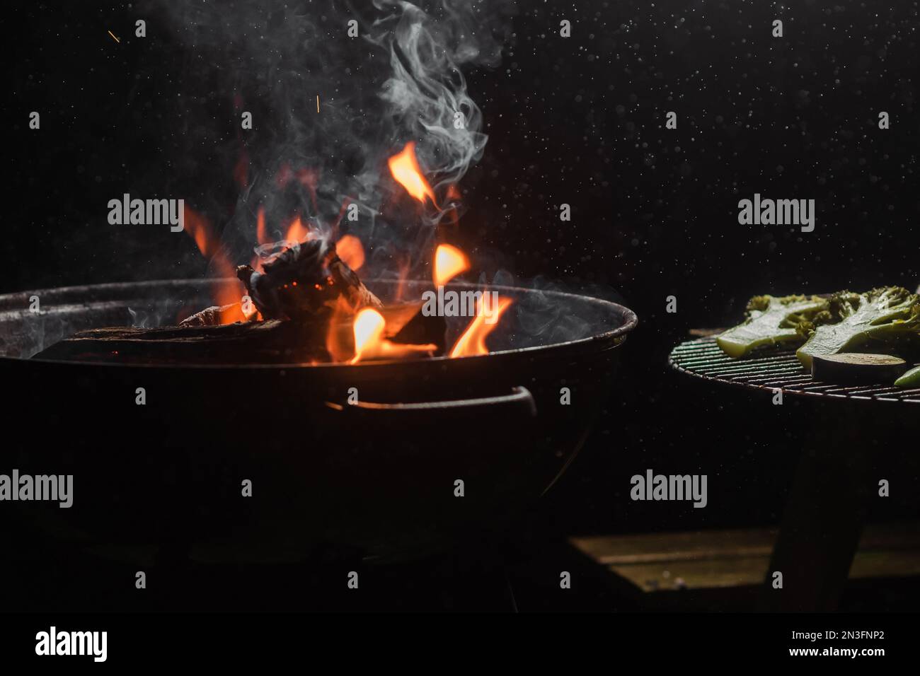 Firewood burns in a round barbecue at night. Dark background. Preparing ...