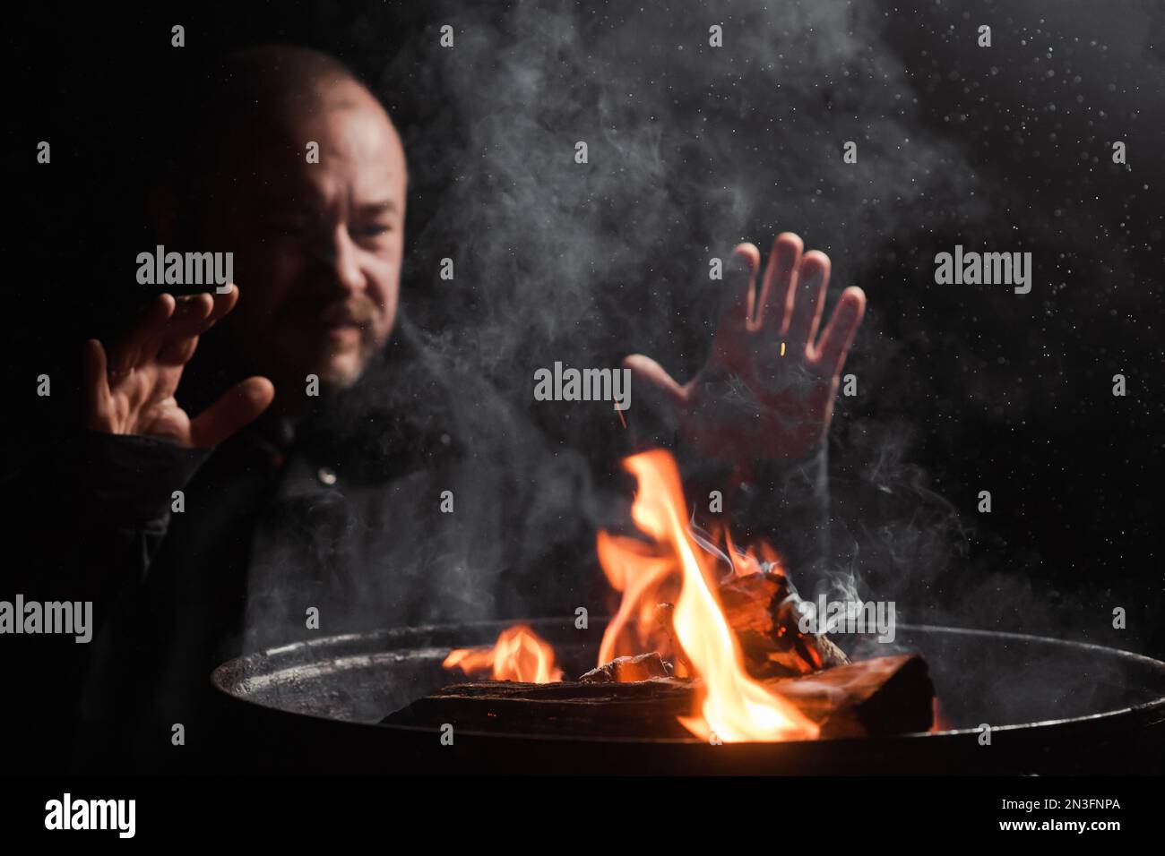A man is warming himself by the fire of a barrel in the dark. Homeless ...