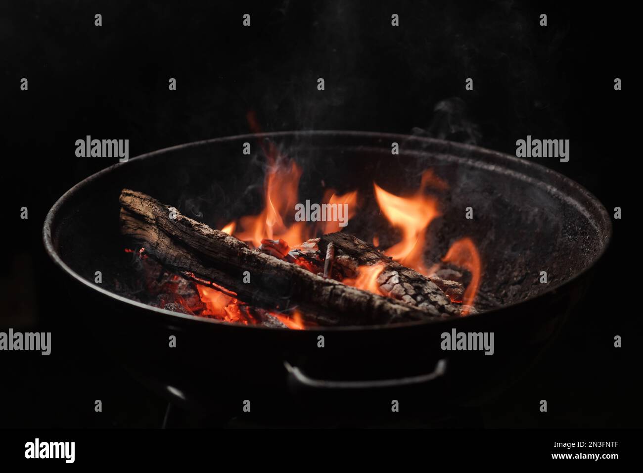 Firewood burns in a round barbecue at night. Dark background. Preparing ...