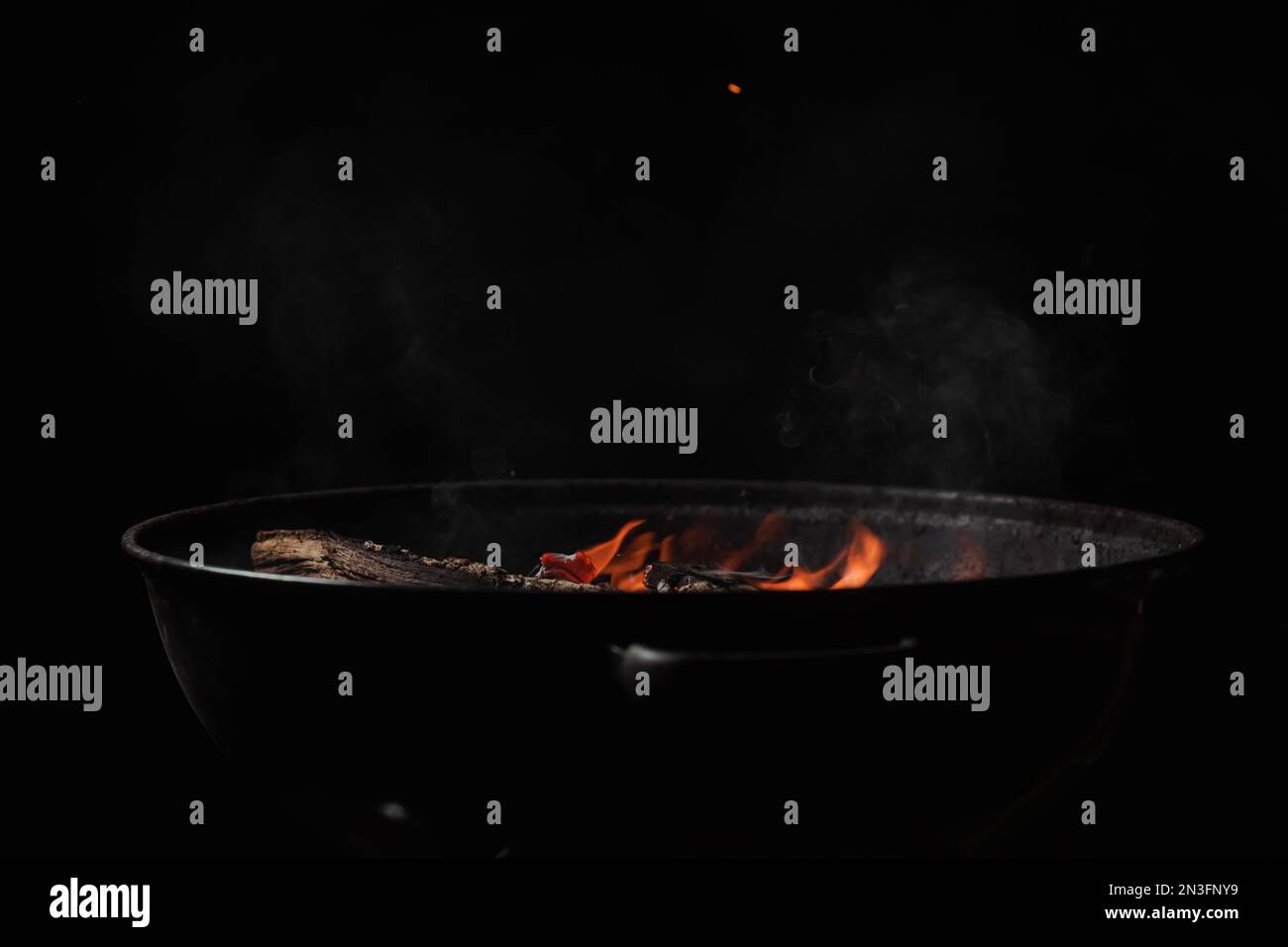Firewood burns in a round barbecue at night. Dark background. Preparing ...