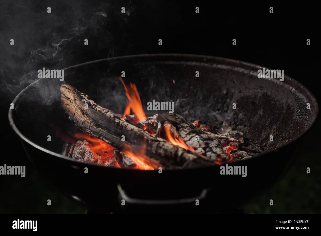 Firewood burns in a round barbecue at night. Dark background. Preparing ...