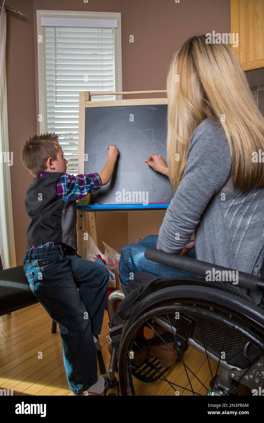 Young paraplegic mother teaching her son and drawing on a chalkboard ...
