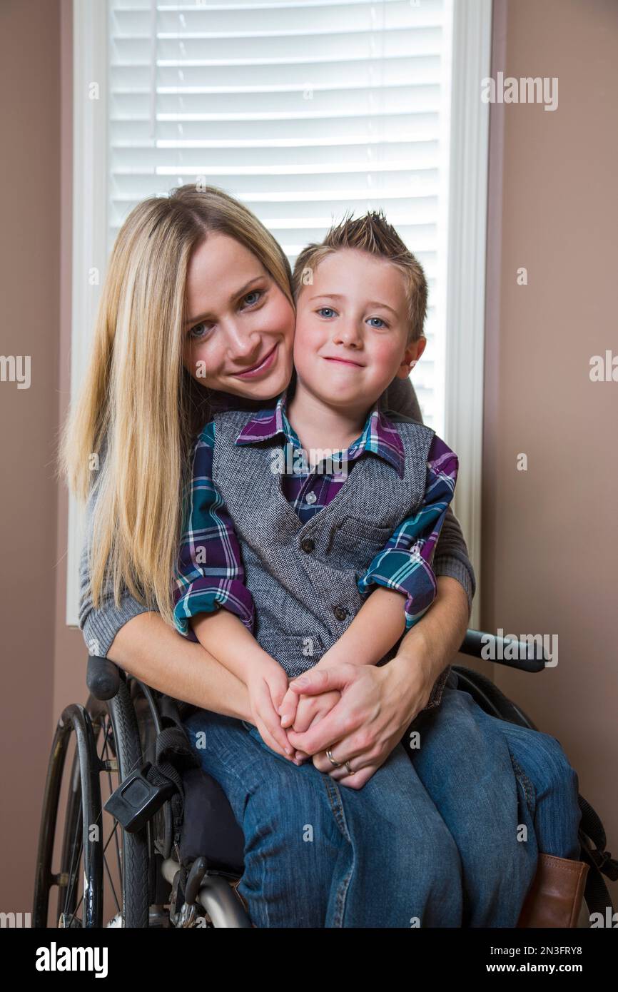 Portrait of young disabled mother with son sitting in her lap at home ...