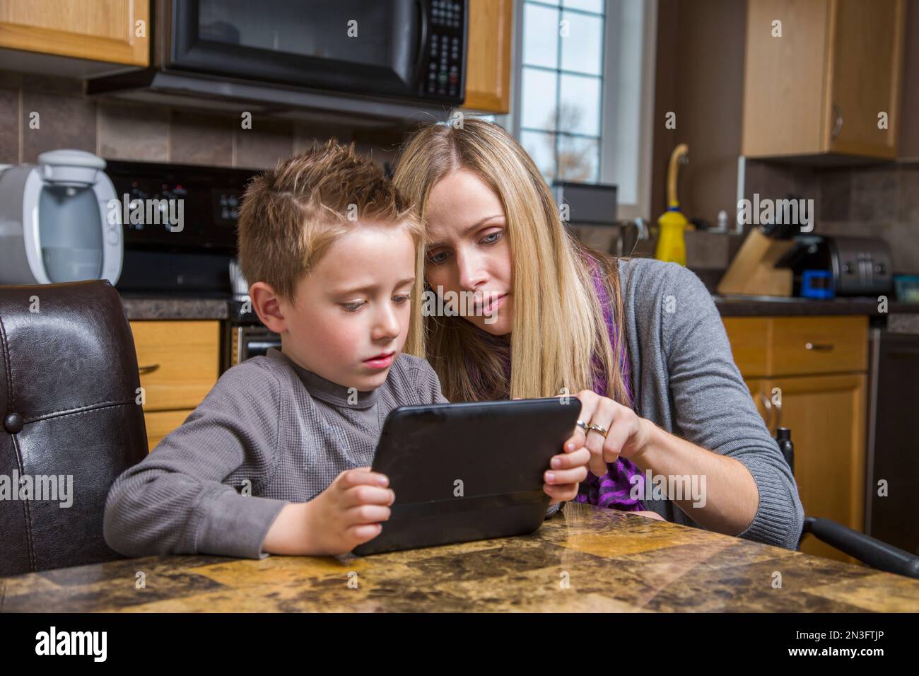 Disabled mother helping her son learn on a tablet at home; Spruce Grove ...