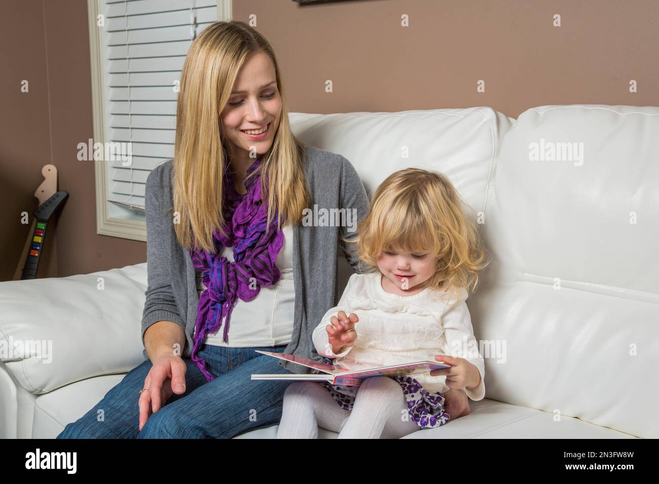 Young disabled mother sits on the couch at home reading to her toddler ...
