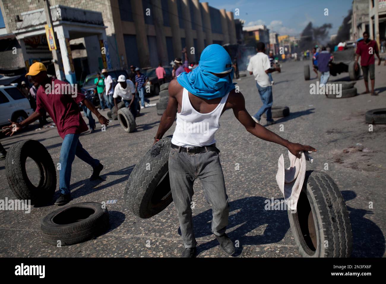 Masked demonstrators roll tires to add to a burning barricade during a ...