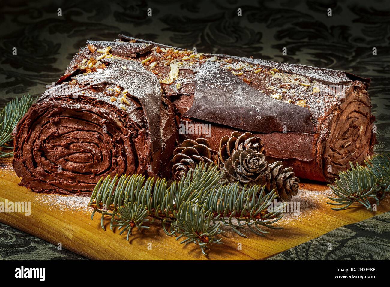 Icing frosted rolled chocolate Yule log cake with evergreen tree pieces ...