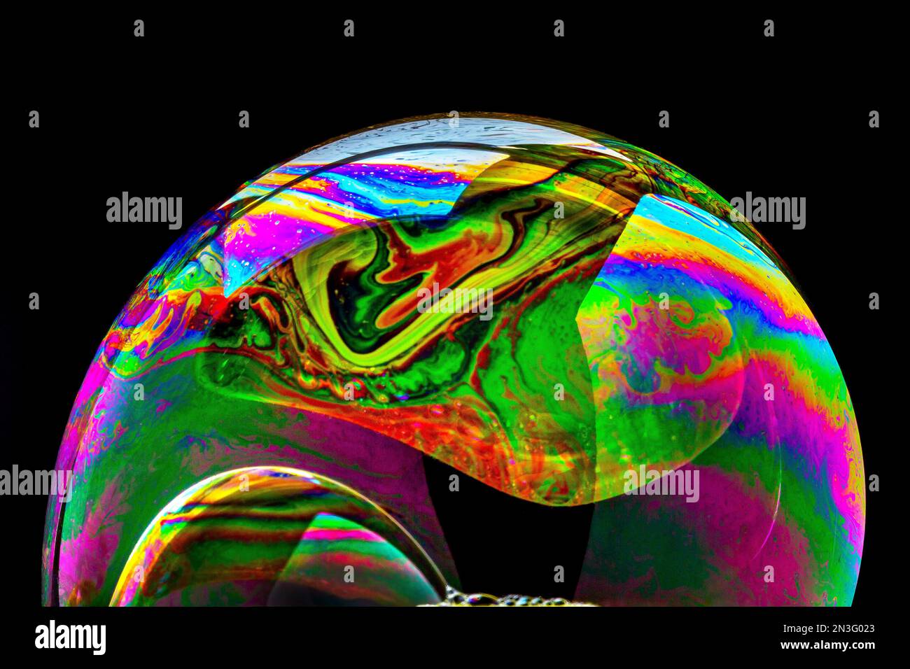 Extreme close-up detail of a very colourful iridescent soap bubble against a black background ...