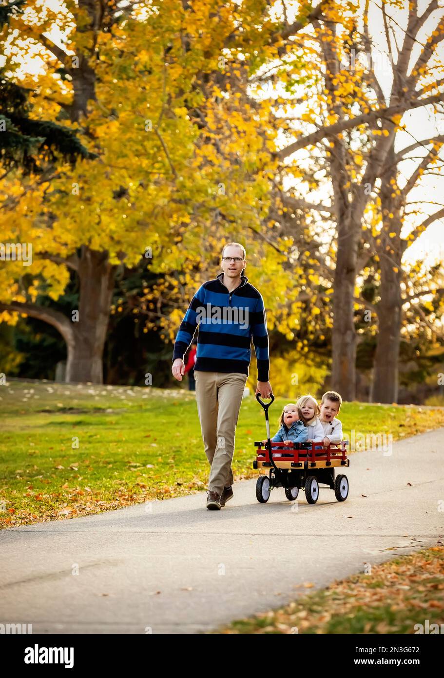 A father pulling his young children in a wagon along a river in a city ...