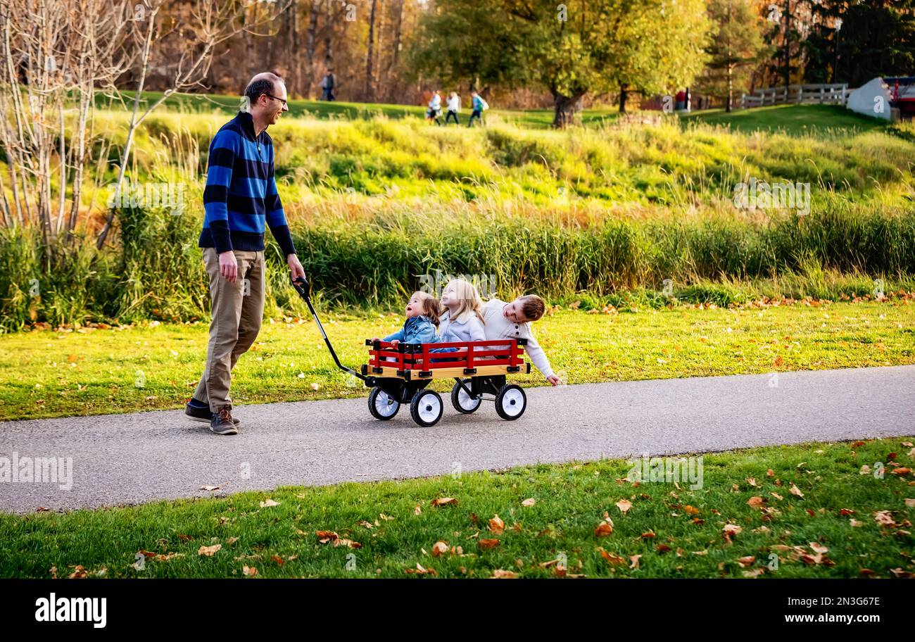 A father pulling his young children in a wagon along a river in a city ...
