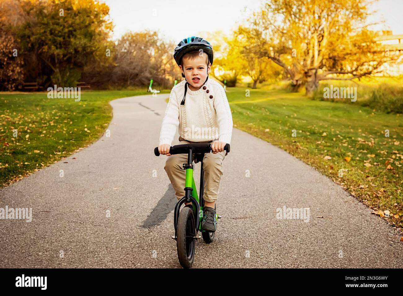 Young boy riding his bike on a path in a city park during a family outing in the fall season; St ...