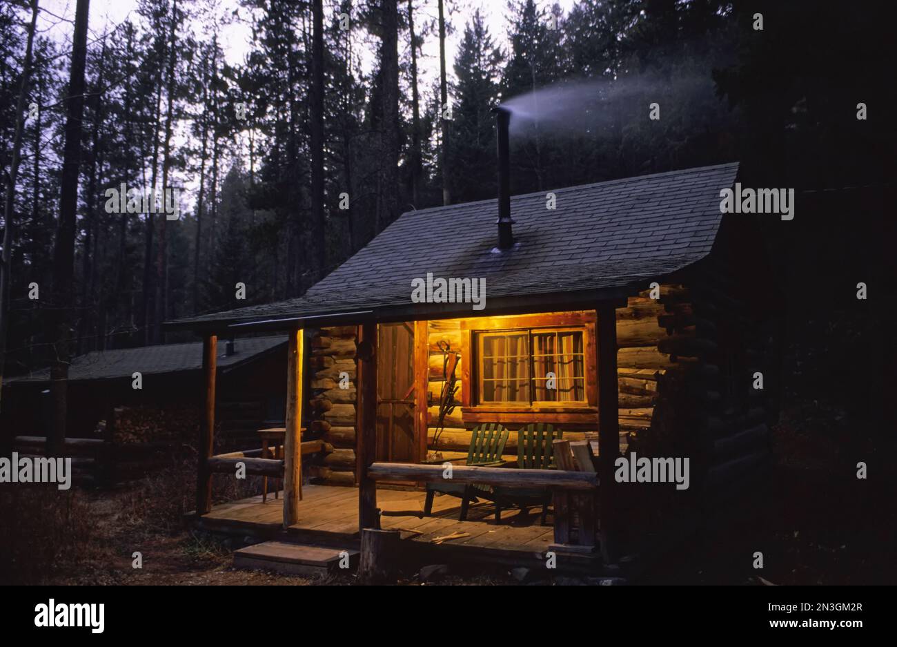 Wood smoke rises from the chimney of a log cabin, near Choteau, Montana ...