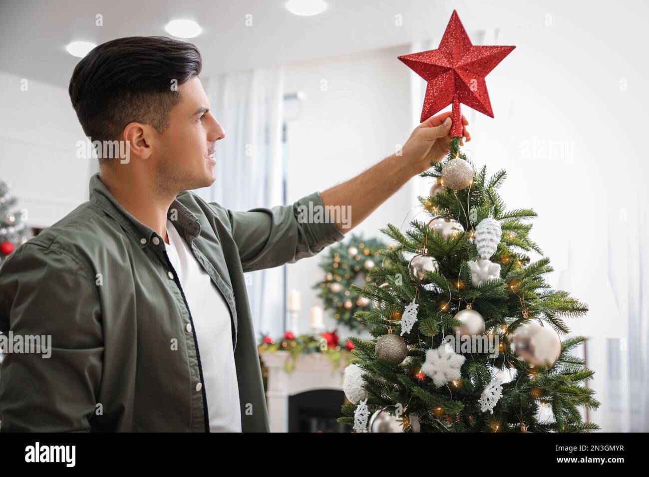Man decorating Christmas tree with star topper indoors Stock Photo - Alamy