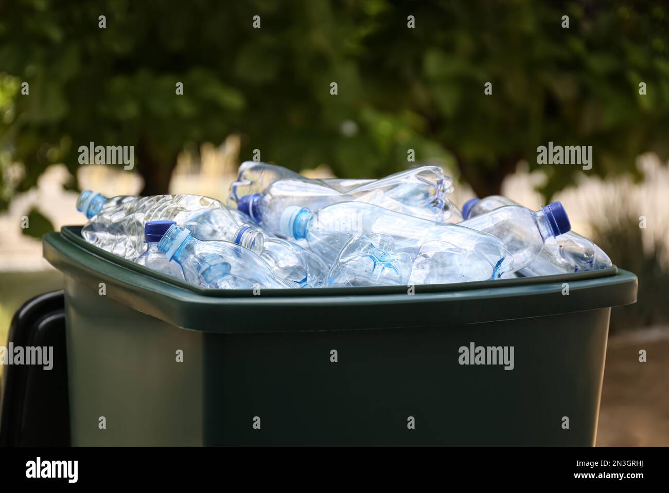 Many used plastic bottles in trash bin outdoors, closeup. Recycling ...