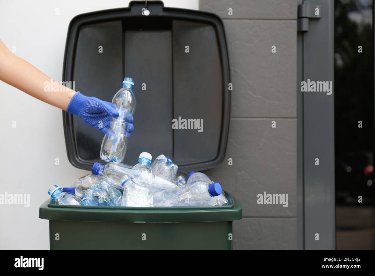 Woman in gloves putting used plastic bottle into trash bin outdoors ...