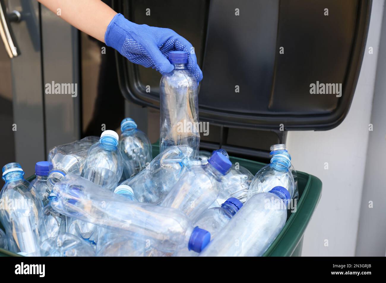 Woman in gloves putting used plastic bottle into trash bin outdoors ...