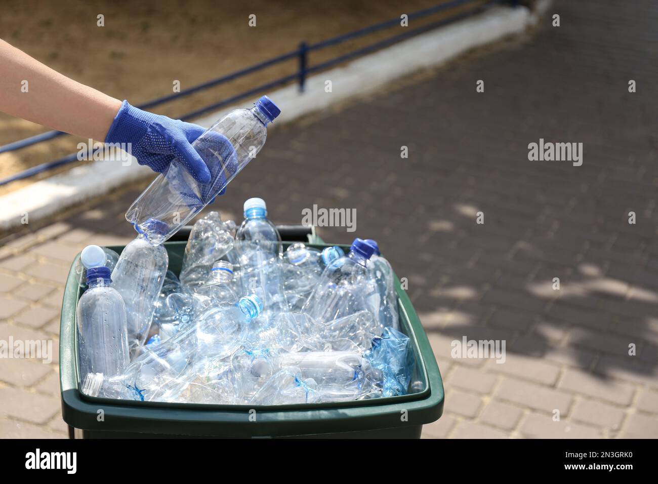 Woman in gloves putting used plastic bottle into trash bin outdoors ...
