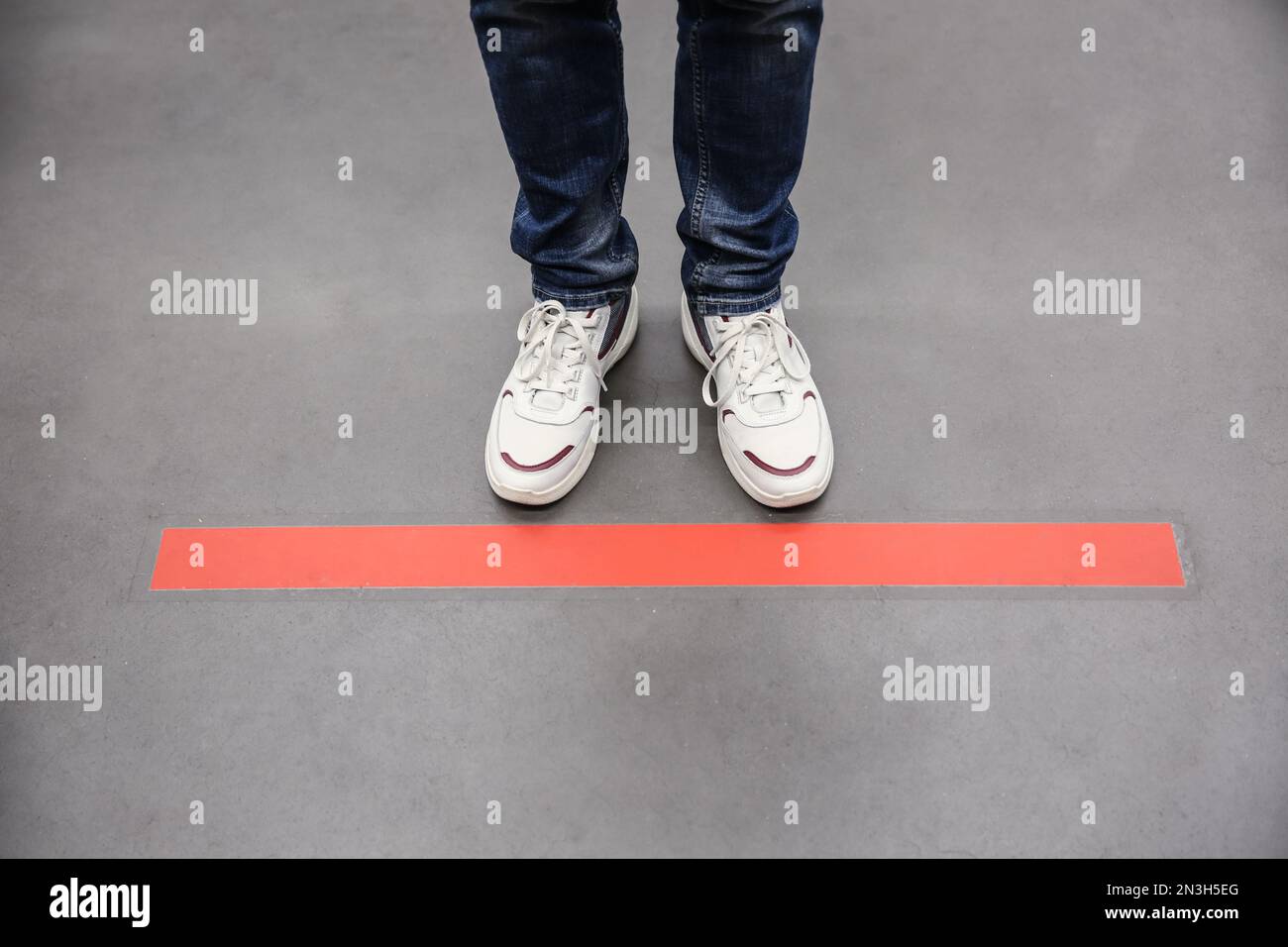 Person standing behind taped floor marking indoors for social distance ...