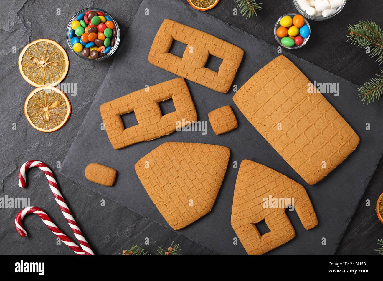 Parts of gingerbread house, fir tree branches and ingredients on black ...