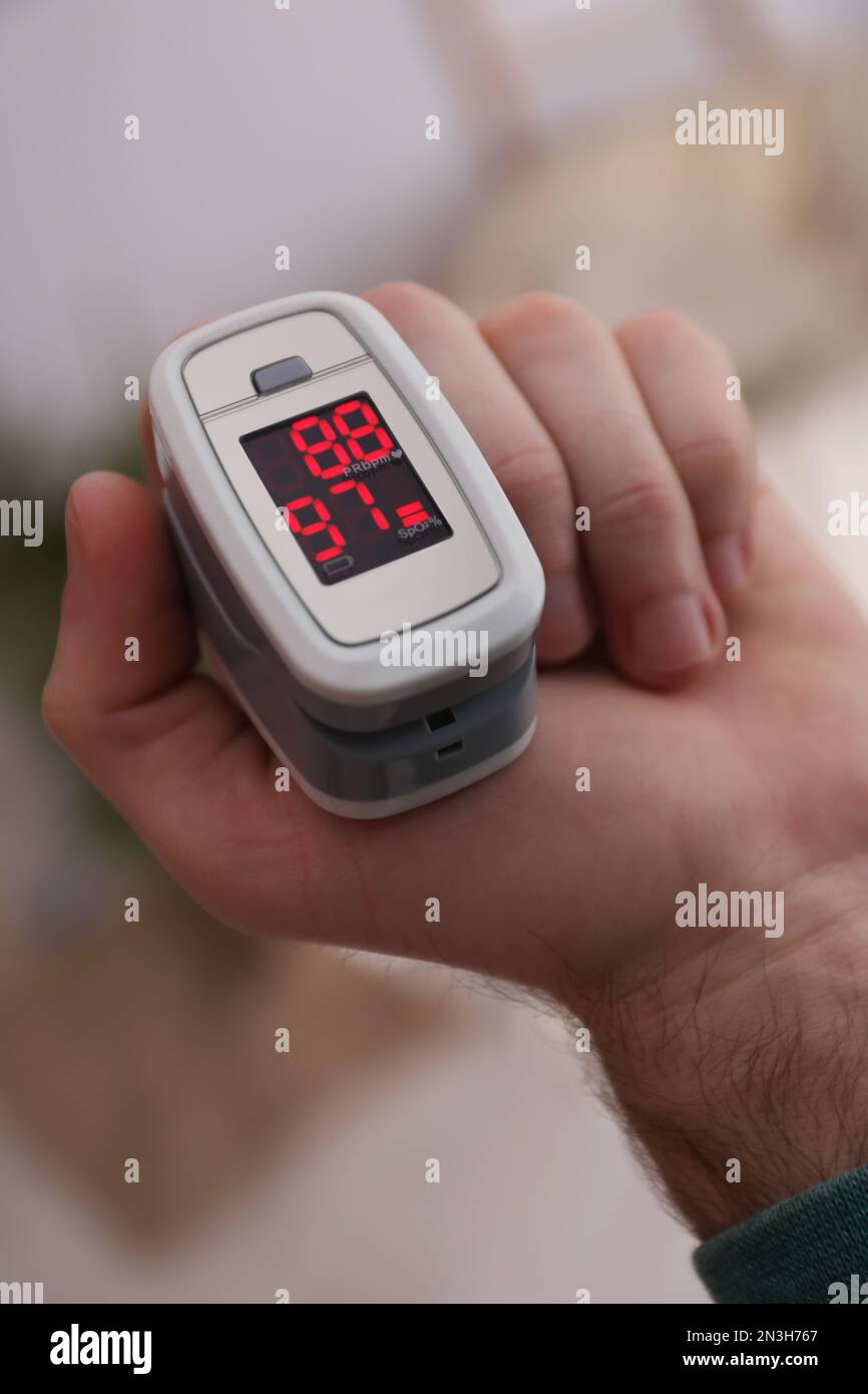 Man measuring oxygen level with modern fingertip pulse oximeter indoors ...