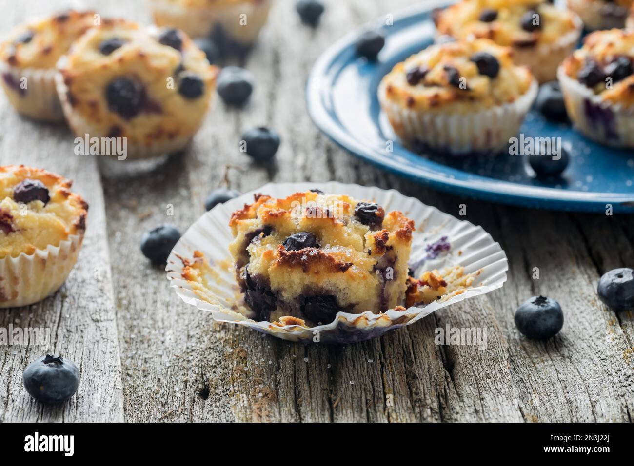 A blueberry muffin with the paper liner peeled back and several in ...