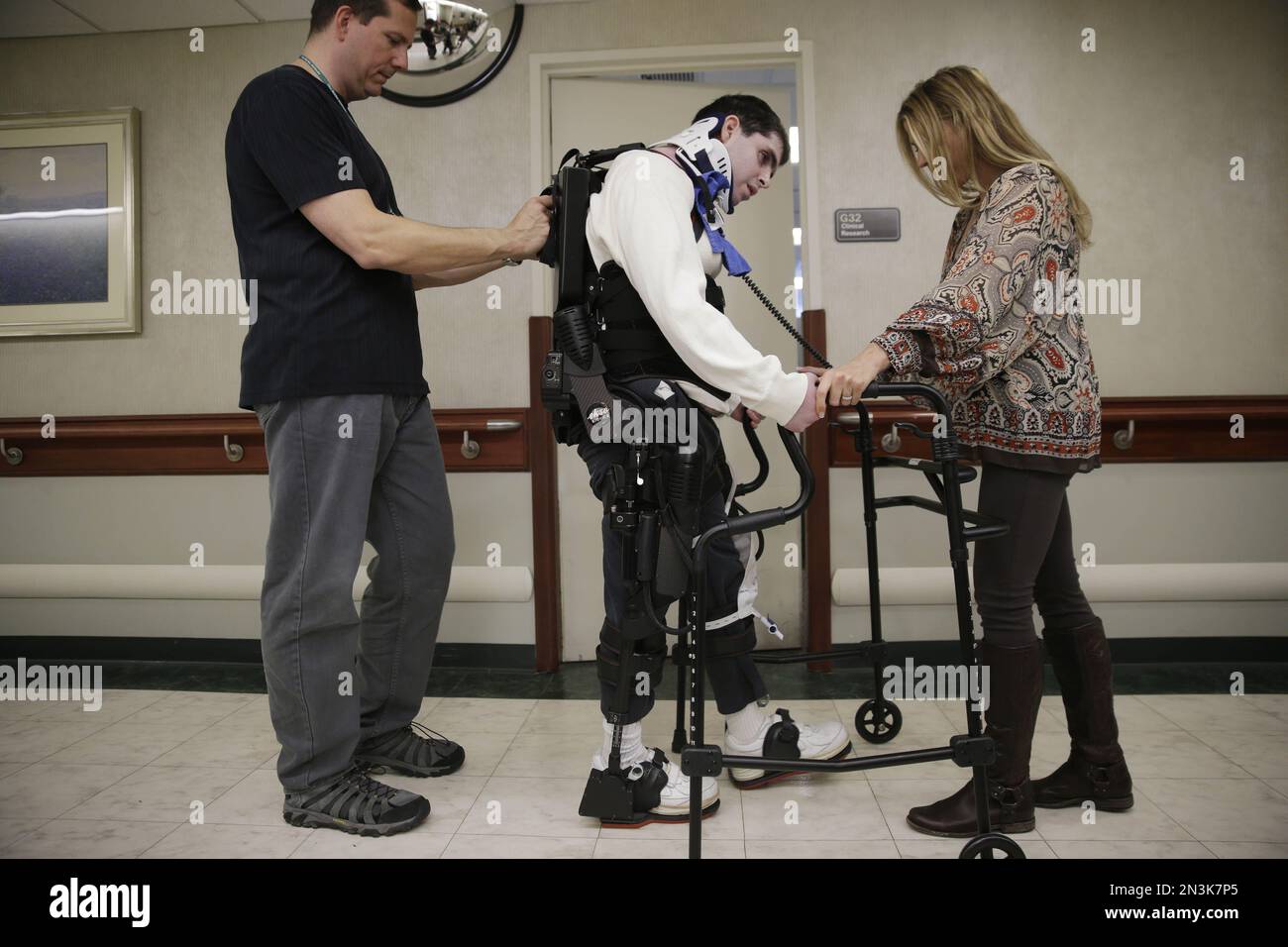 James Cody, 29, center, walks with the aid of a bionic exoskeleton and ...