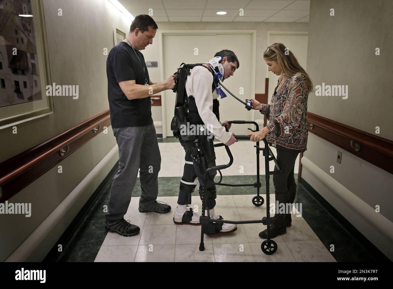 James Cody, 29, center, walks with the aid of a bionic exoskeleton and ...