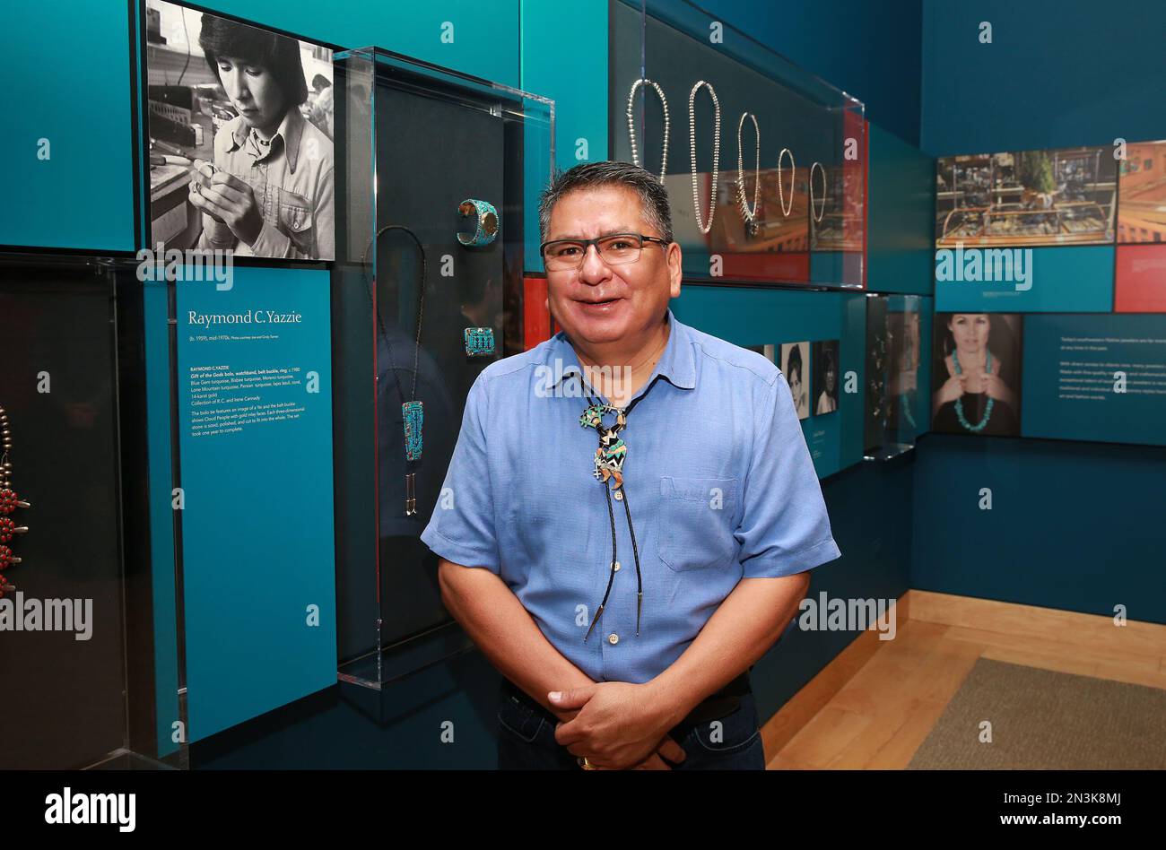 Jeweler Raymond C. Yazzie (Navajo) poses next to a photo of his younger ...