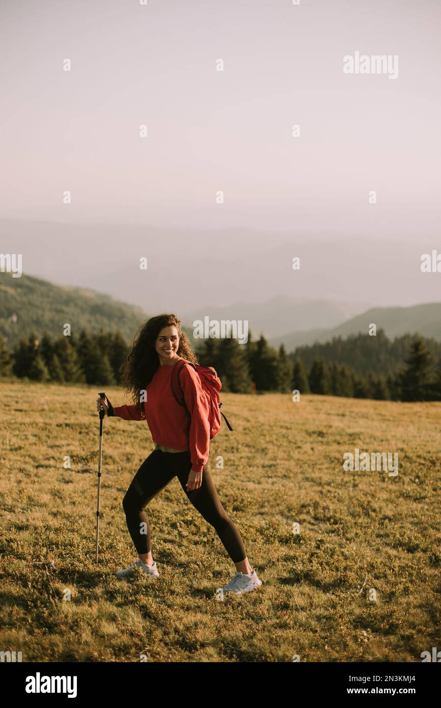 Young woman is taking a scenic hike on a hill, carrying all her ...