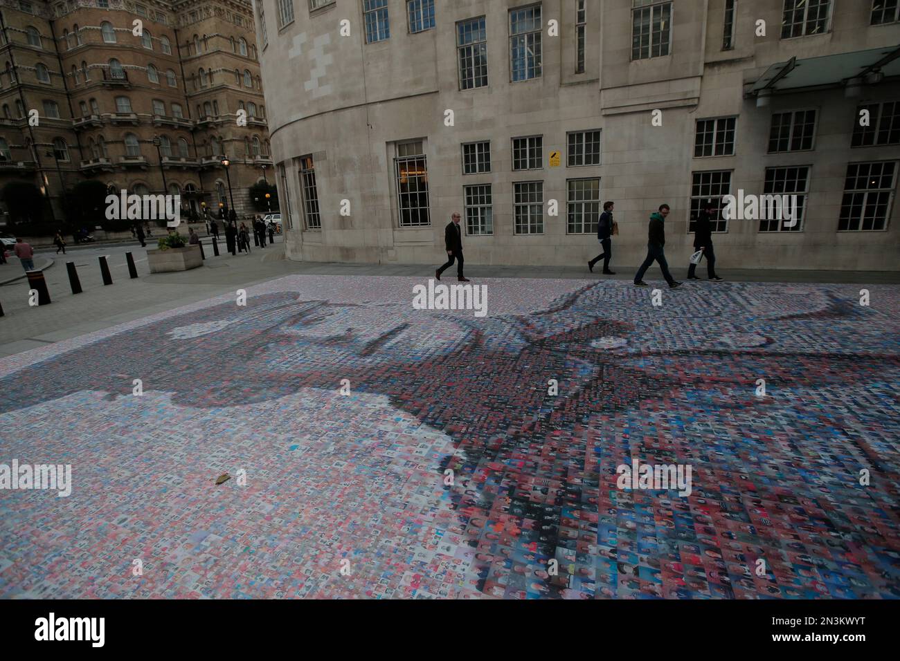People walk past a digital mosaic of photographs of people, depicting ...