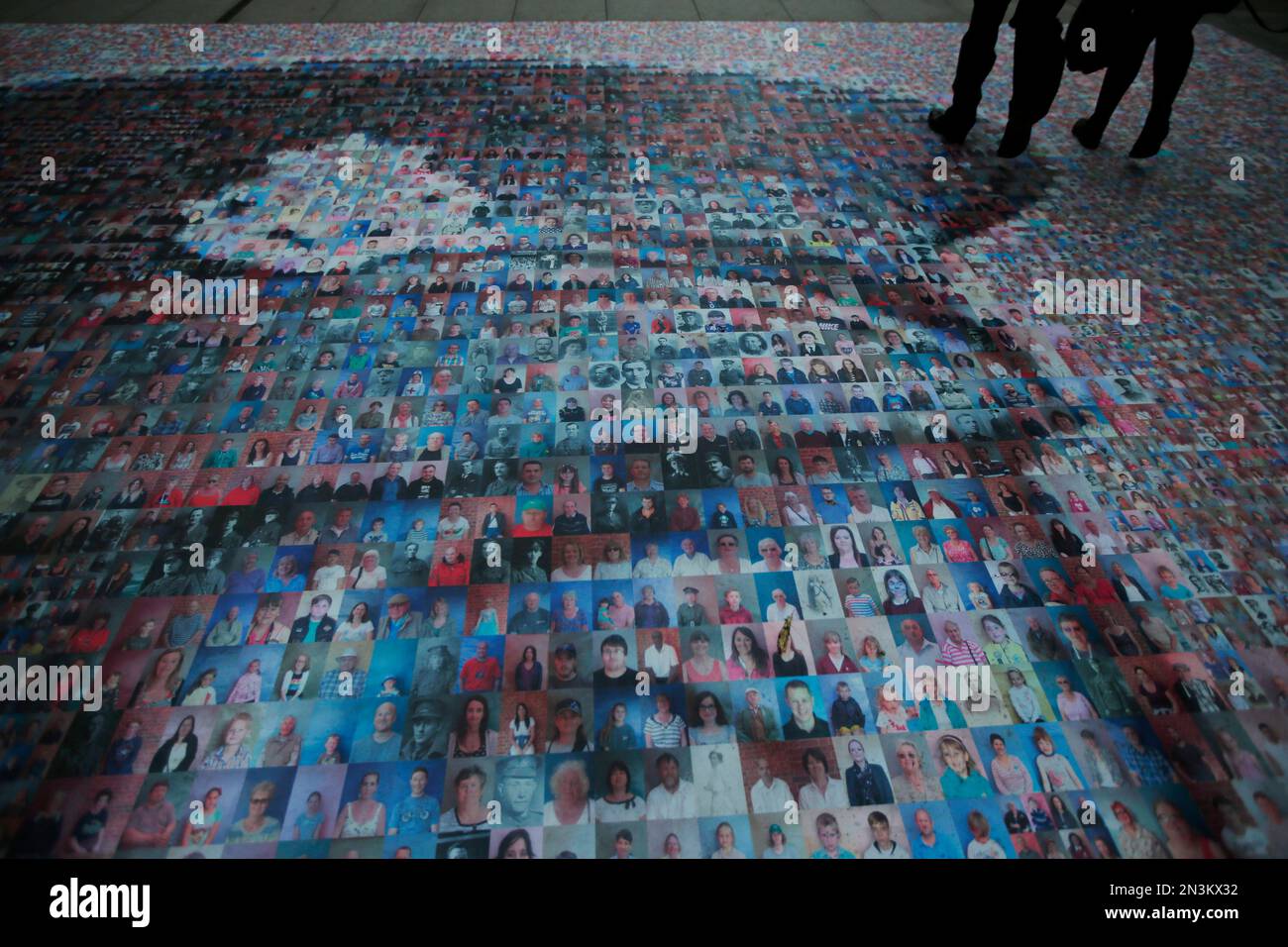 People walk on a digital mosaic of photographs of people, depicting ...