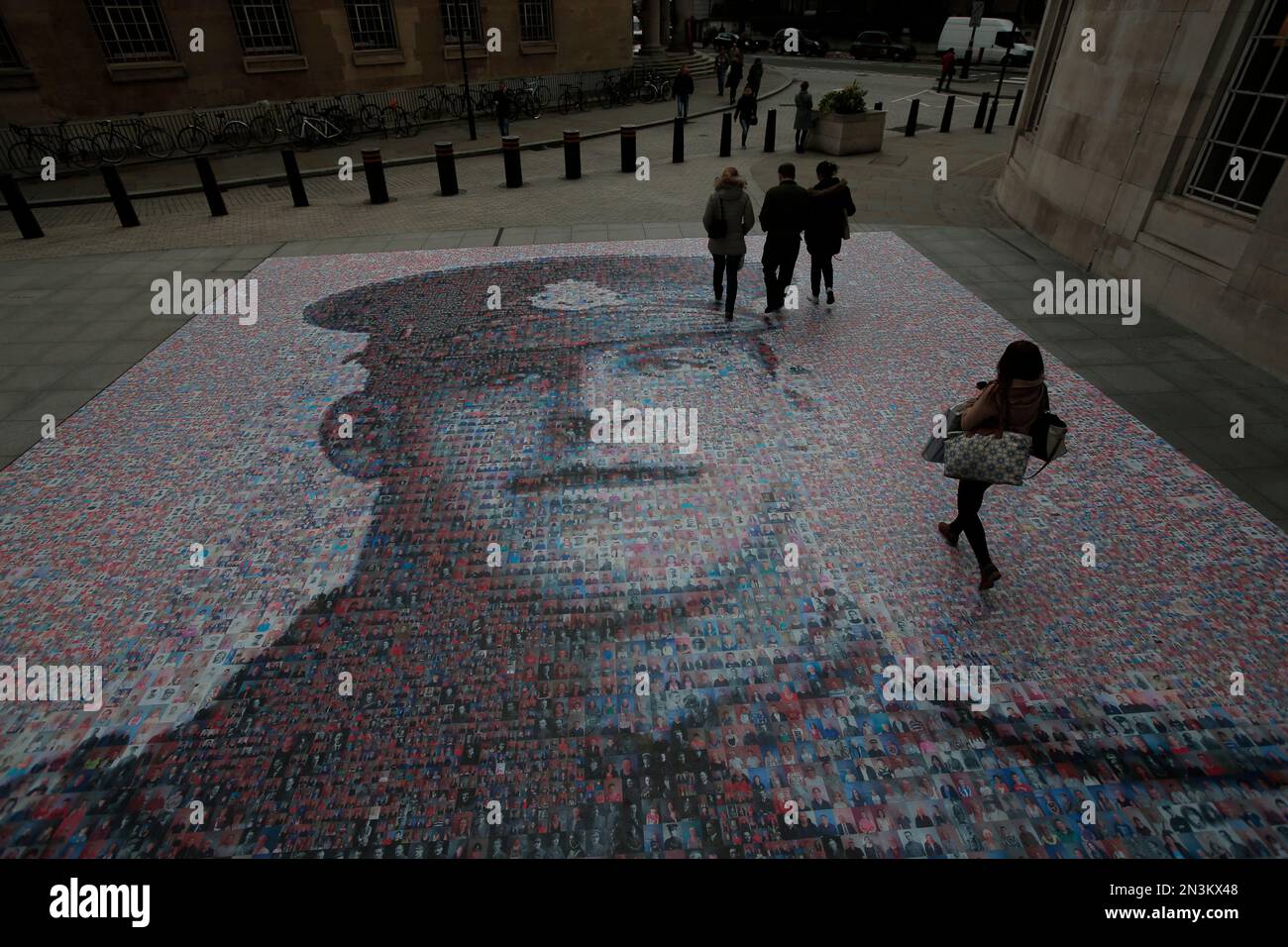 People walk on and past a digital mosaic of photographs of people ...