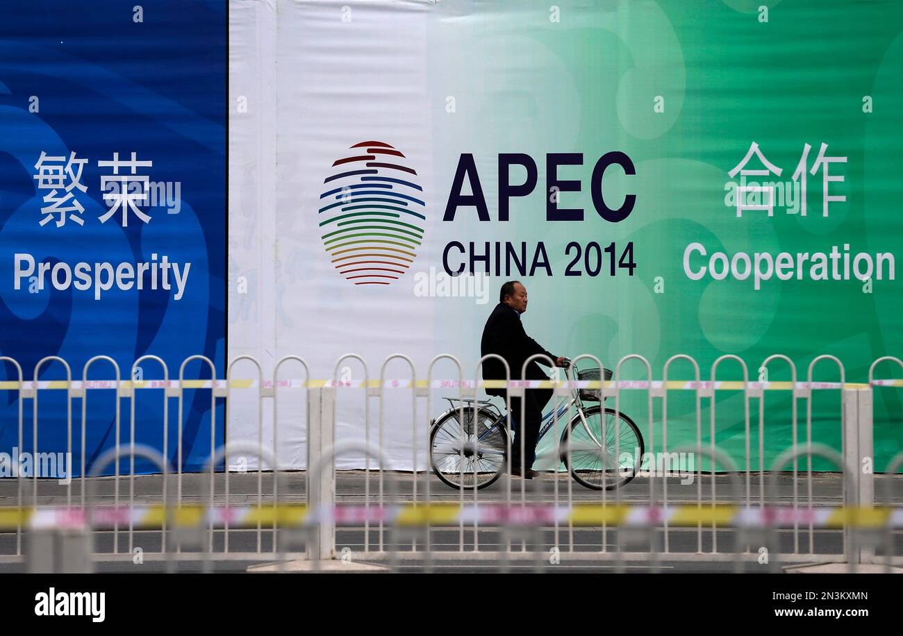 A man rides a bicycle past a billboard of APEC China 2014 with its ...