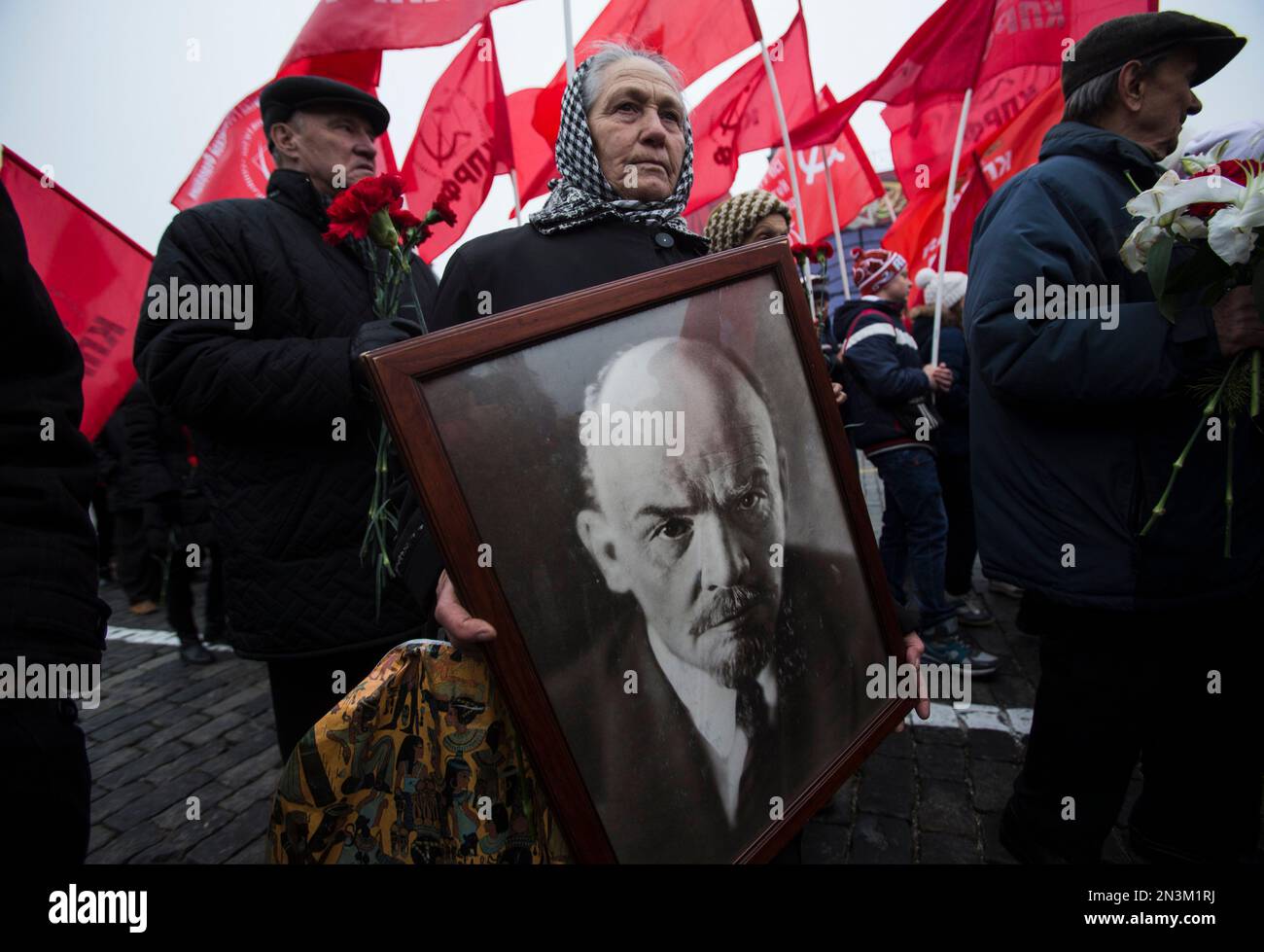 A woman carries a portrait of Lenin as she walks with the Communist ...