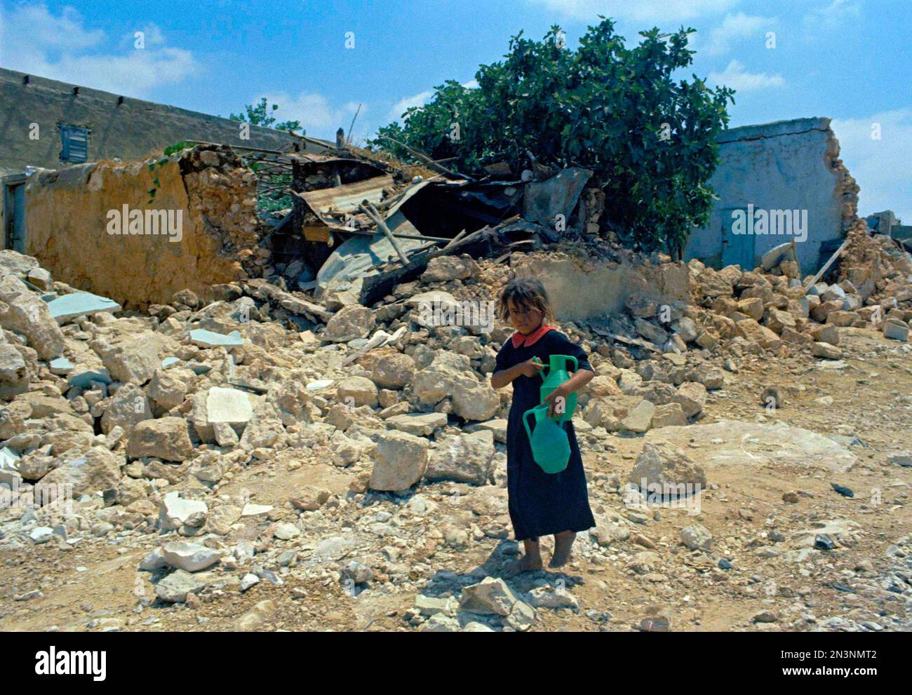 A young Arab girl carrying pitchers wanders through the debris of some ...