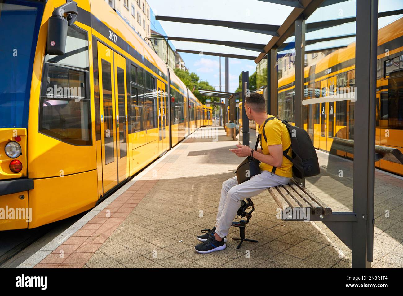 A guy in a yellow T-shirt is waiting for his tram at a public stop ...