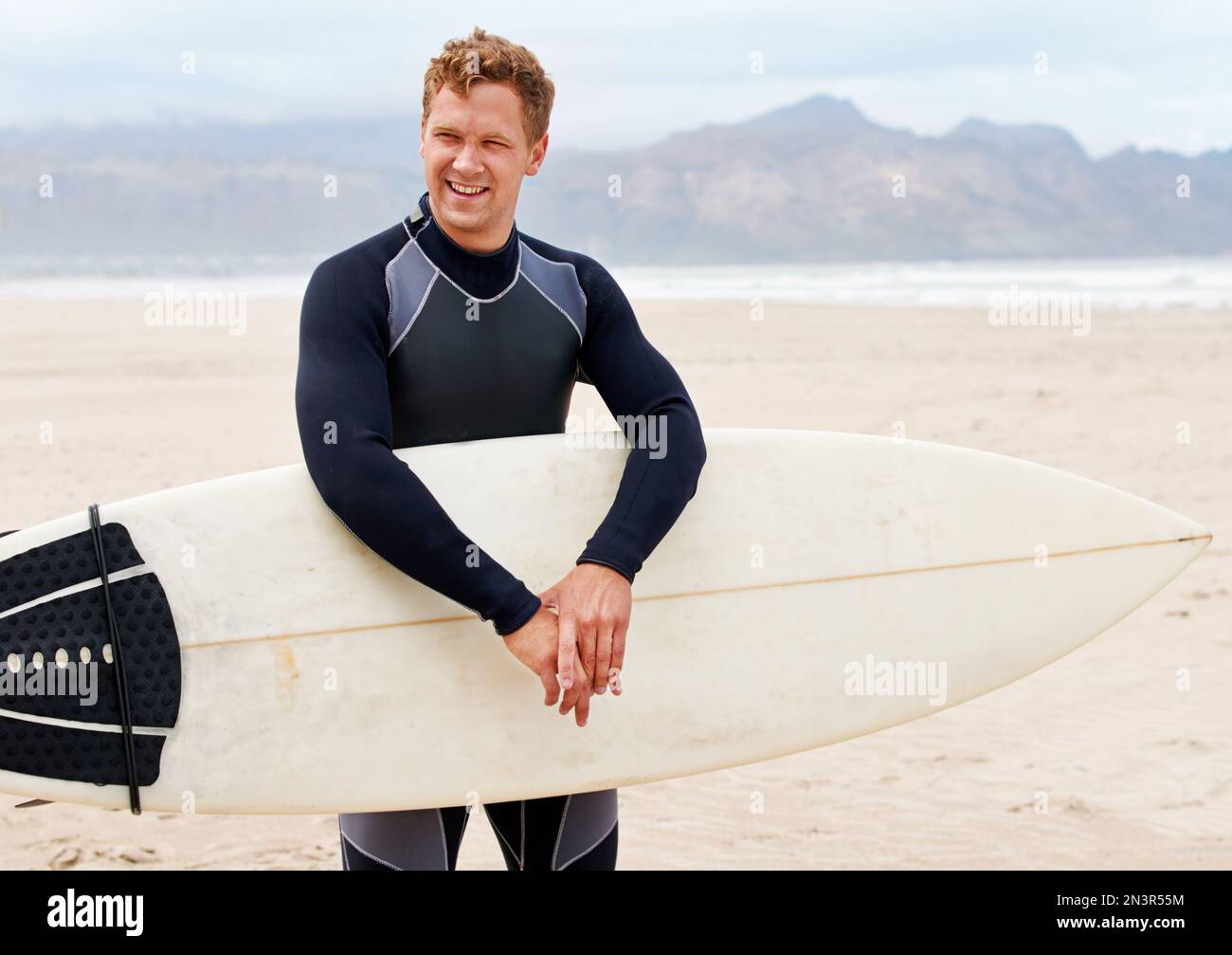 Ready to hit the waves. A young surfer smiling as he holds his ...