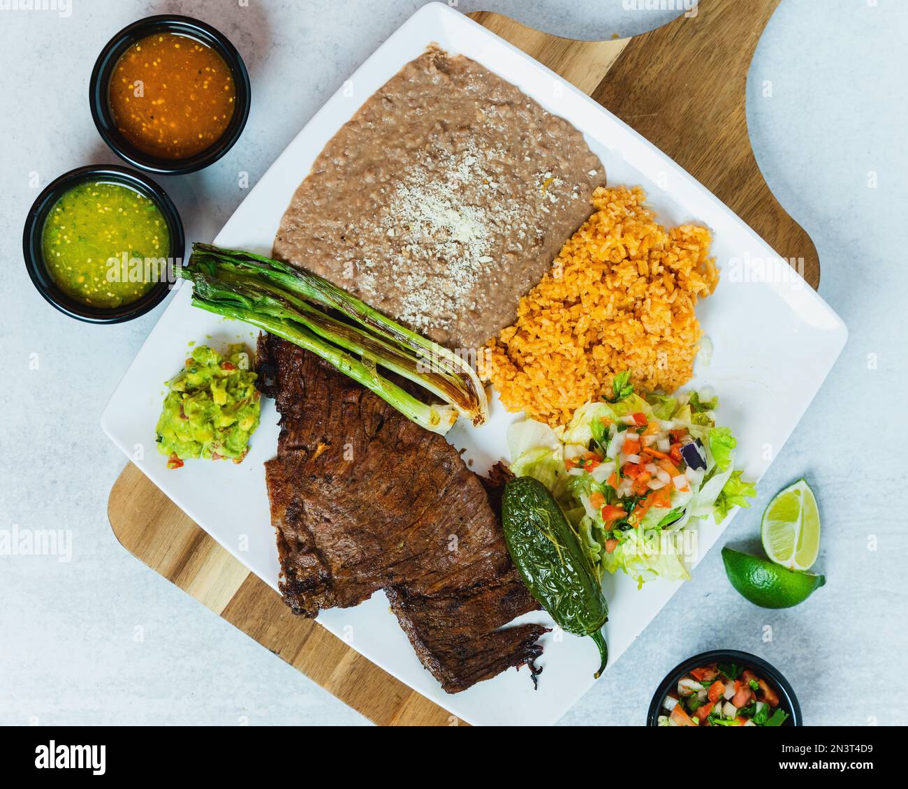 A top view of bistek carne asada plate on a wooden board with refried ...